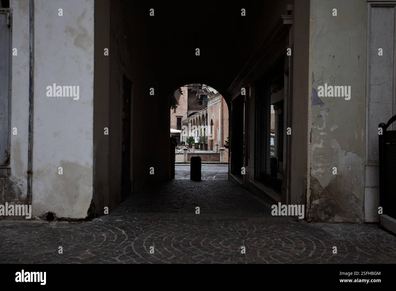 Cobbled archway in the shade under a building that leads to a square in ...