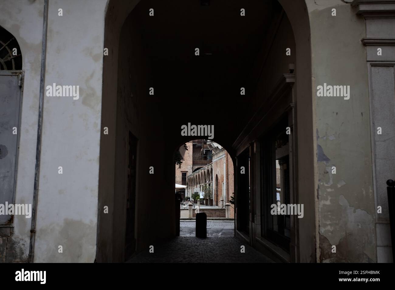 Cobbled archway in the shade under a building that leads to a square in ...