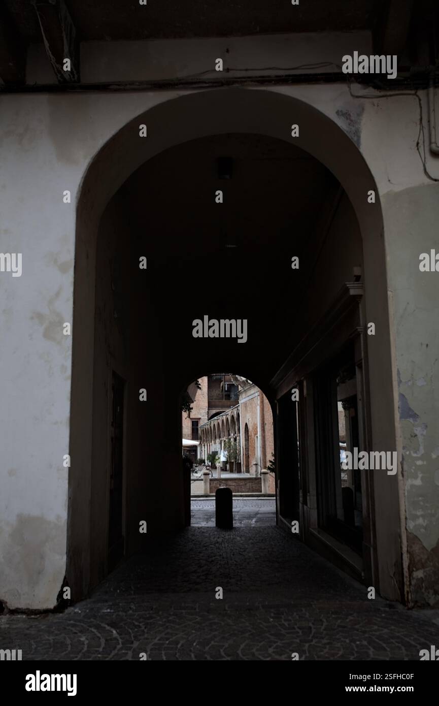 Cobbled archway in the shade under a building that leads to a square in ...