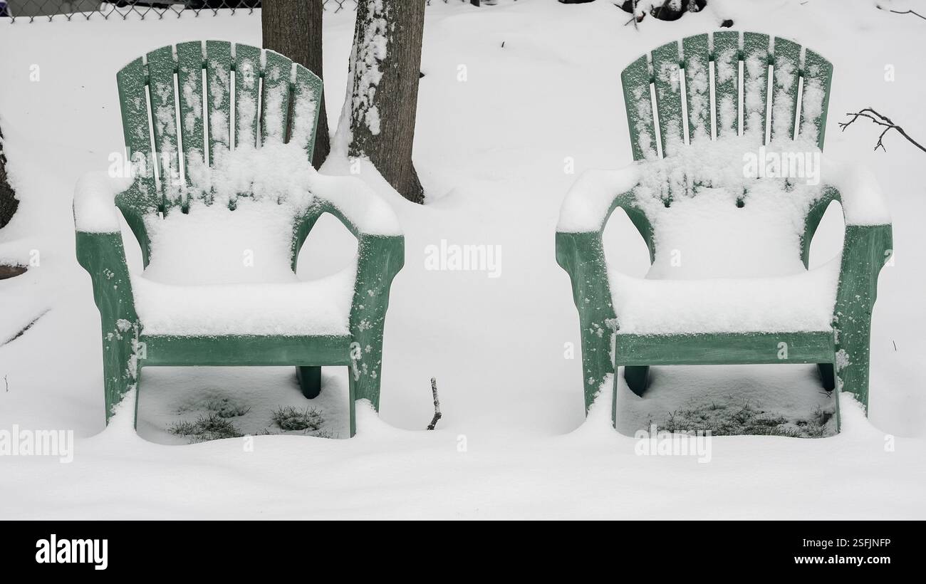 Two green chairs sit side by side, blanketed with white snow in a ...
