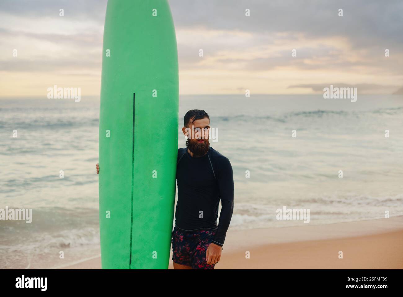 Young handsome male surfer with a surfboard is enjoying a view while ...
