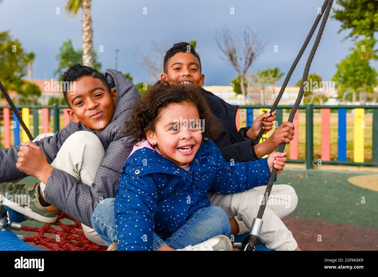 Three siblings enjoying a playful moment together on a swing in a playground Stock Photo - Alamy