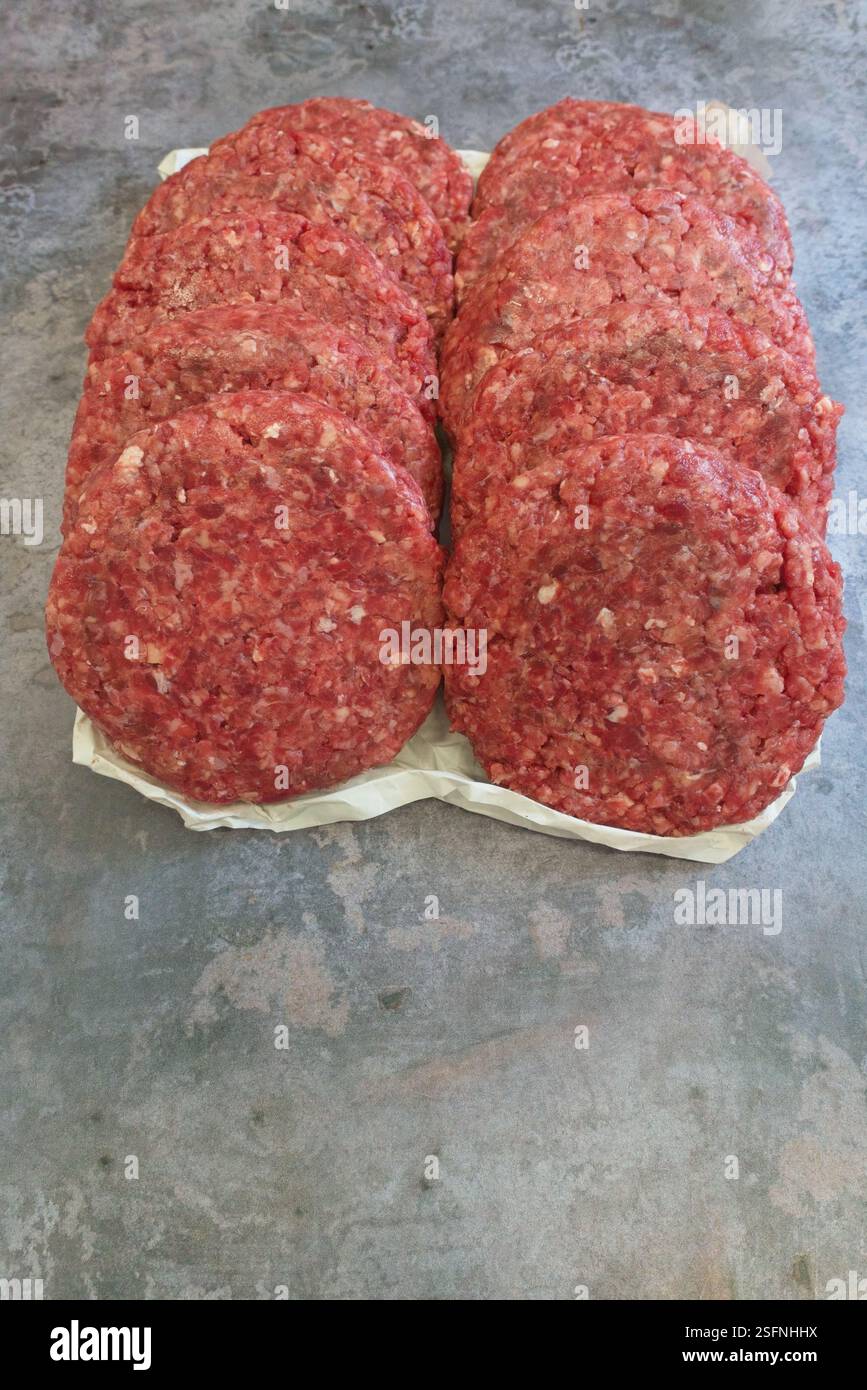 Raw beef burgers sit on paper resting atop a concrete table, viewed ...
