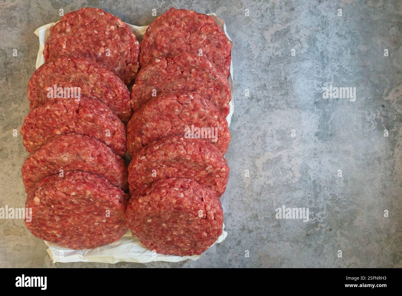 Raw beef burgers rested on paper atop a concrete table, captured from ...