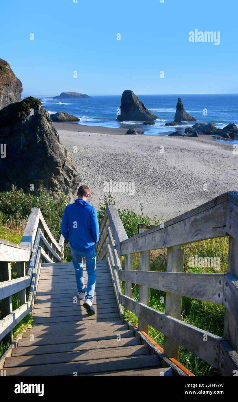 Man climbs down the wooden walkway to Bandon Beach, Oregon. He has on a ...