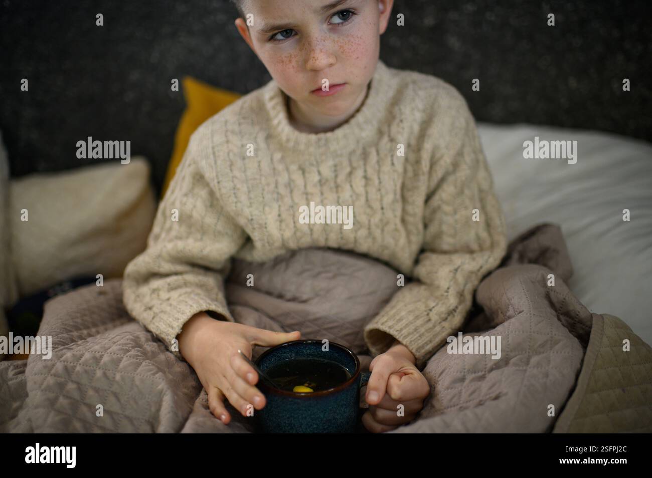 The boy sits in bed, holding a mug of hot tea with lemon Stock Photo ...