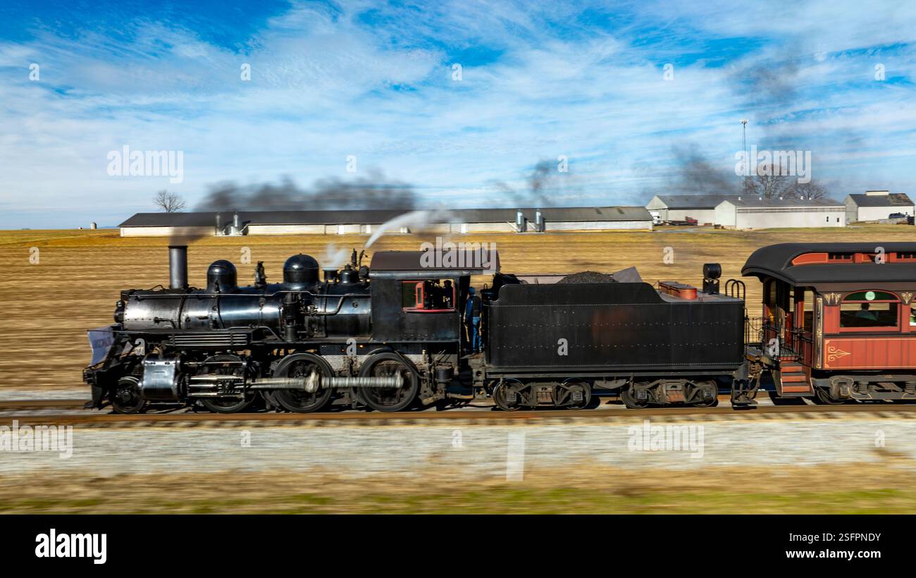 A vintage steam locomotive powers along the tracks, sending plumes of ...