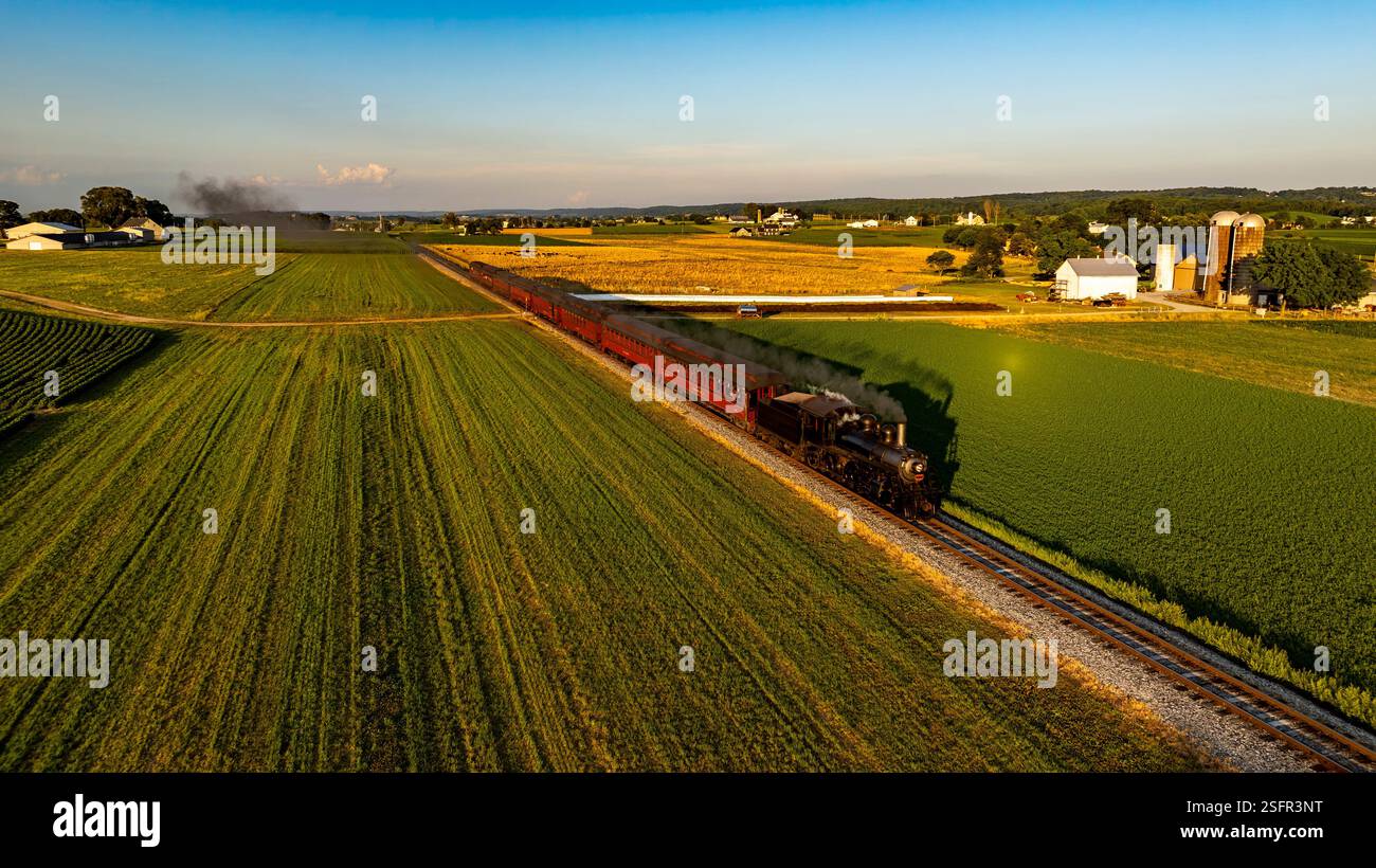 A steam train chugs along the tracks, billowing smoke into the evening ...