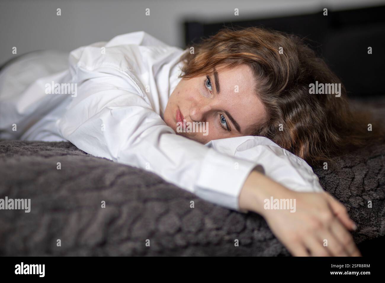 Sad Woman With Blue Eyes Lying On A Bed Wearing A White Shirt Stock