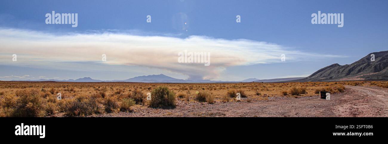 A panoramic view shows smoke rising into the clear blue sky above a dry ...