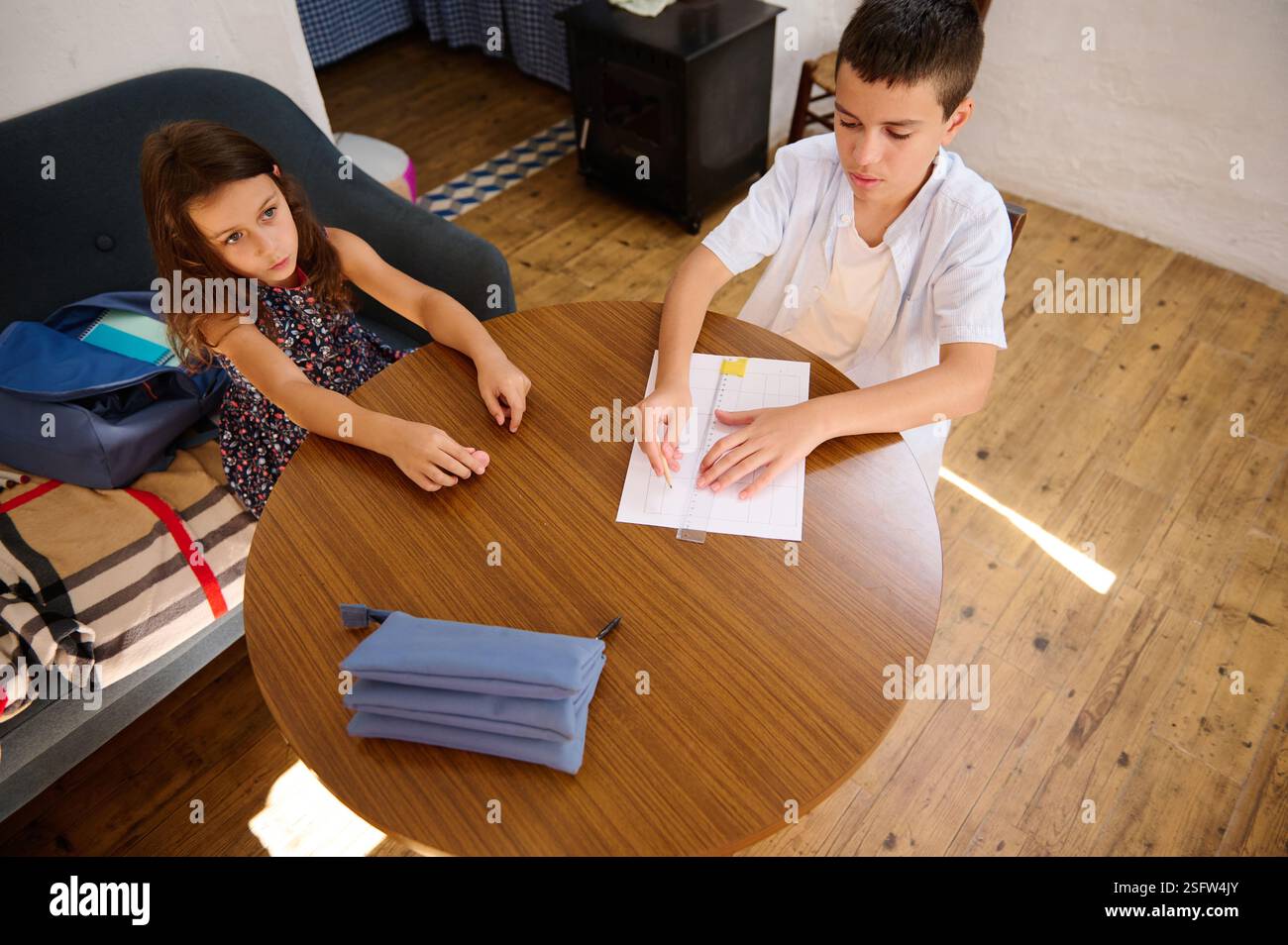 Two children sit at a round wooden table, collaborating on an ...