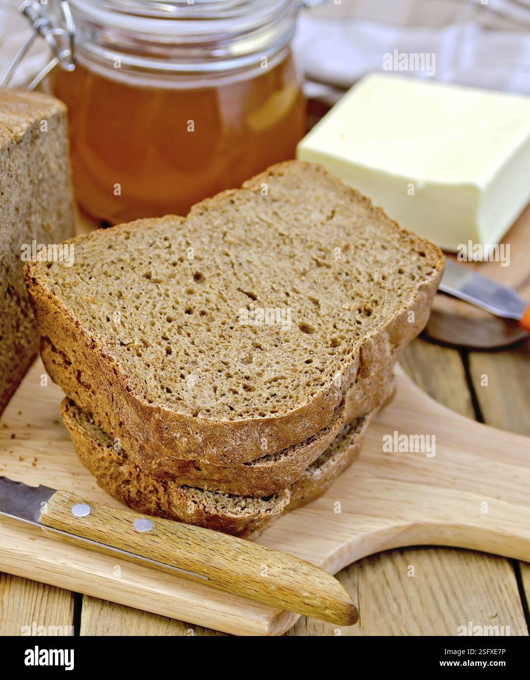 A stack of slices of rye homemade bread with a knife, napkin, a jar of ...