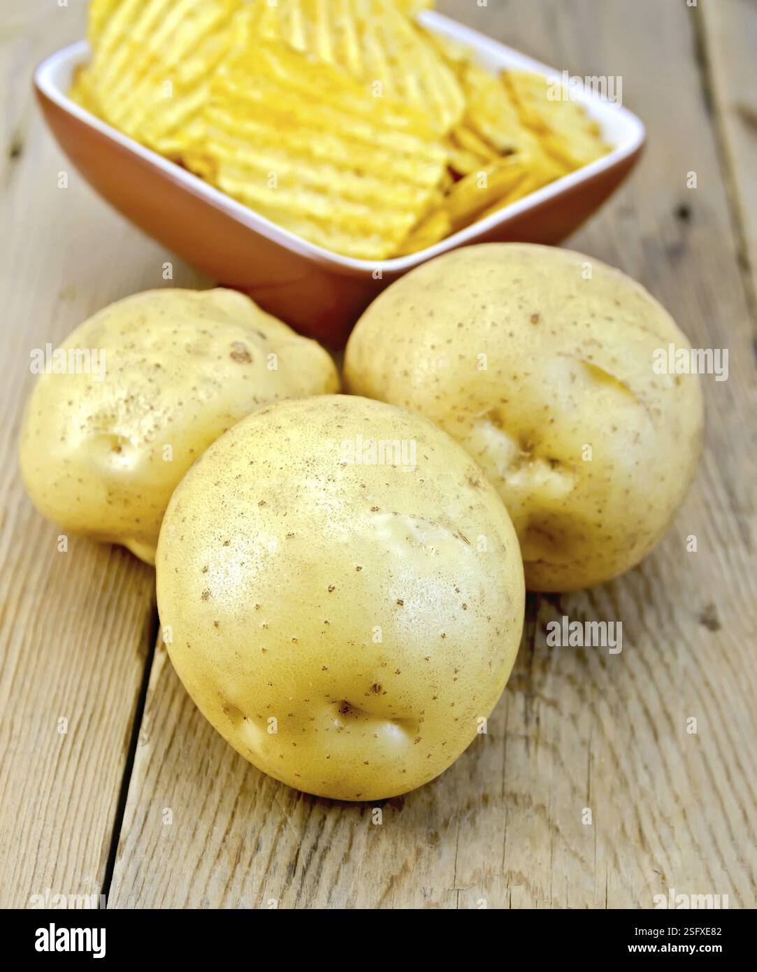 Three fresh yellow potato tuber, potato chips in a clay bowl on a ...