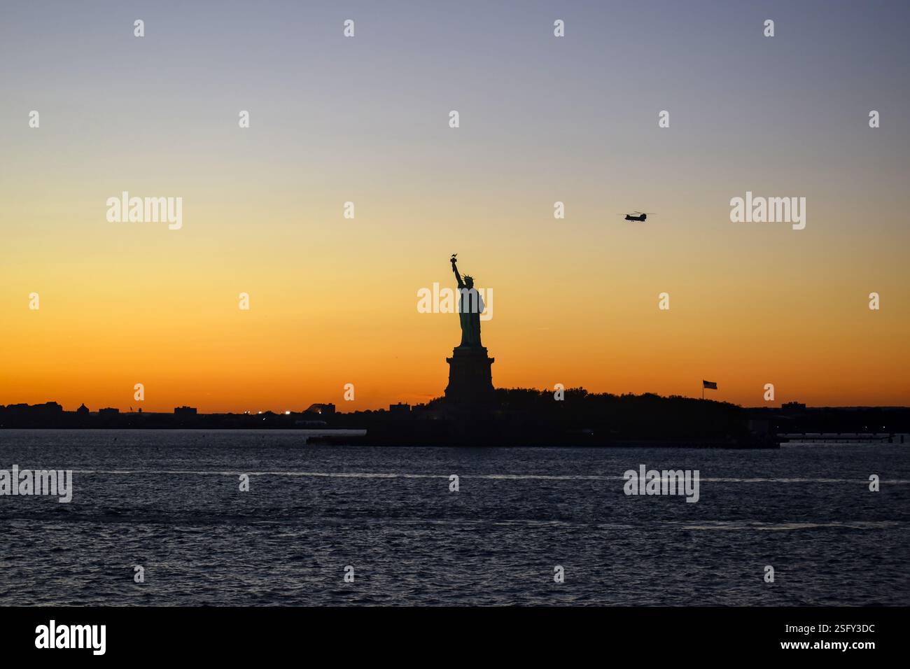 The Statue of Liberty glows at sunset as a U.S. Army Chinook helicopter ...