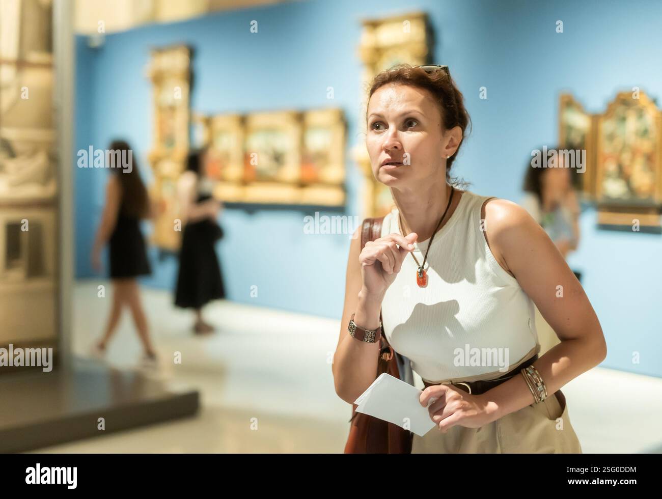 Focused woman visitor holds booklet with an exhibition program while ...