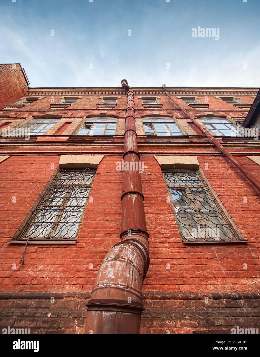 Old brick house with rusty rainwater pipe. Looking up at the brown ...