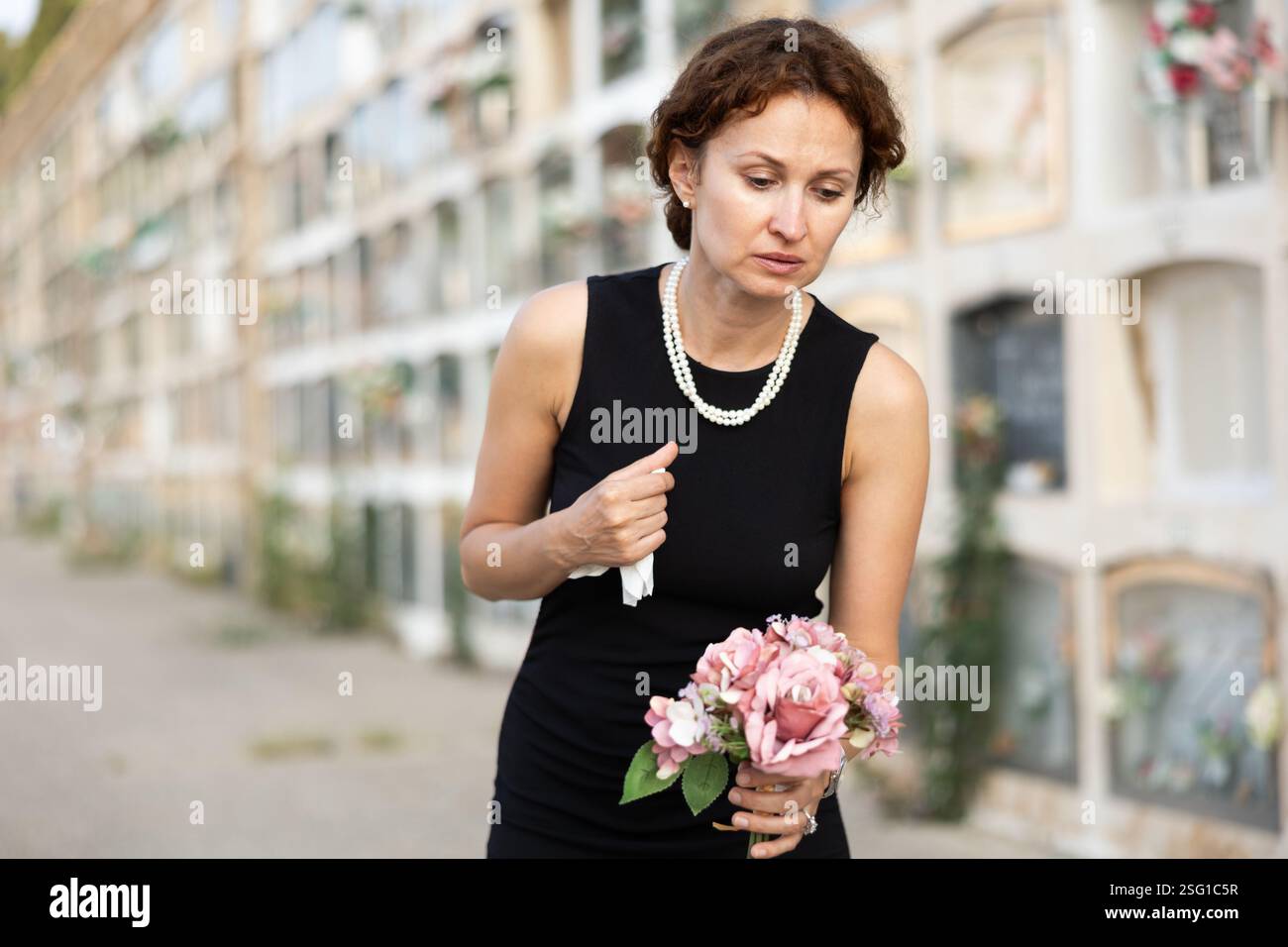 Sad widow in black lays bouquet of flowers on her dead husband grave ...