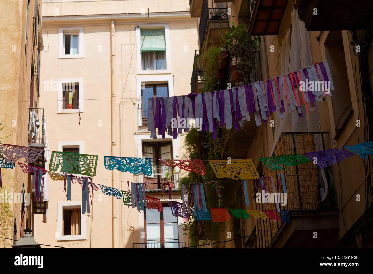 Colorful papel picado banners hang between buildings in a narrow street ...