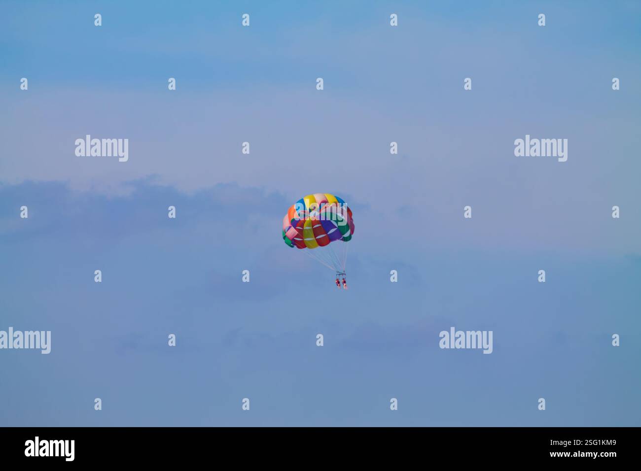 A colorful parachute with two people soaring high in the sky against a ...