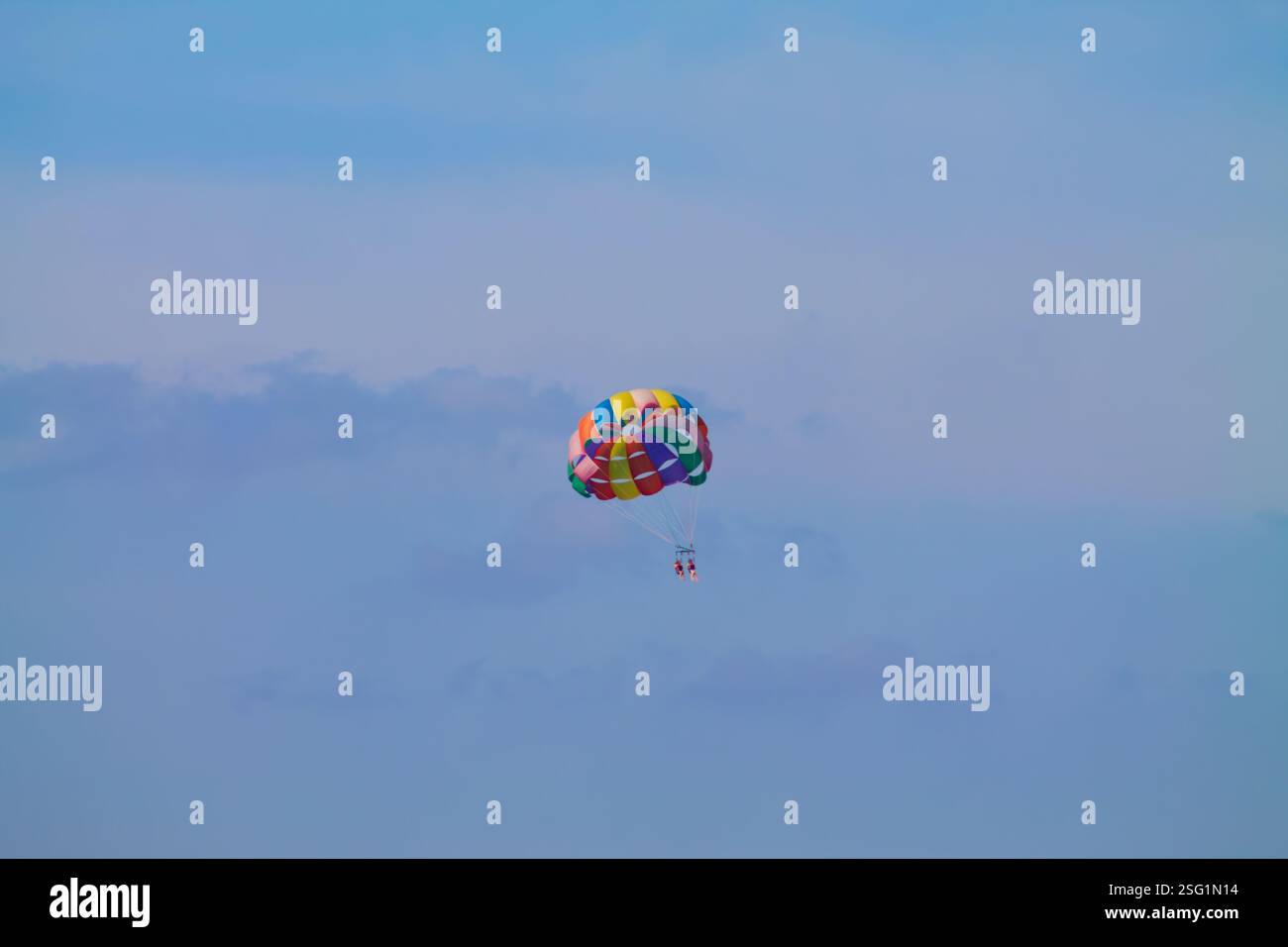 A colorful parachute with two people soaring high in the sky against a ...