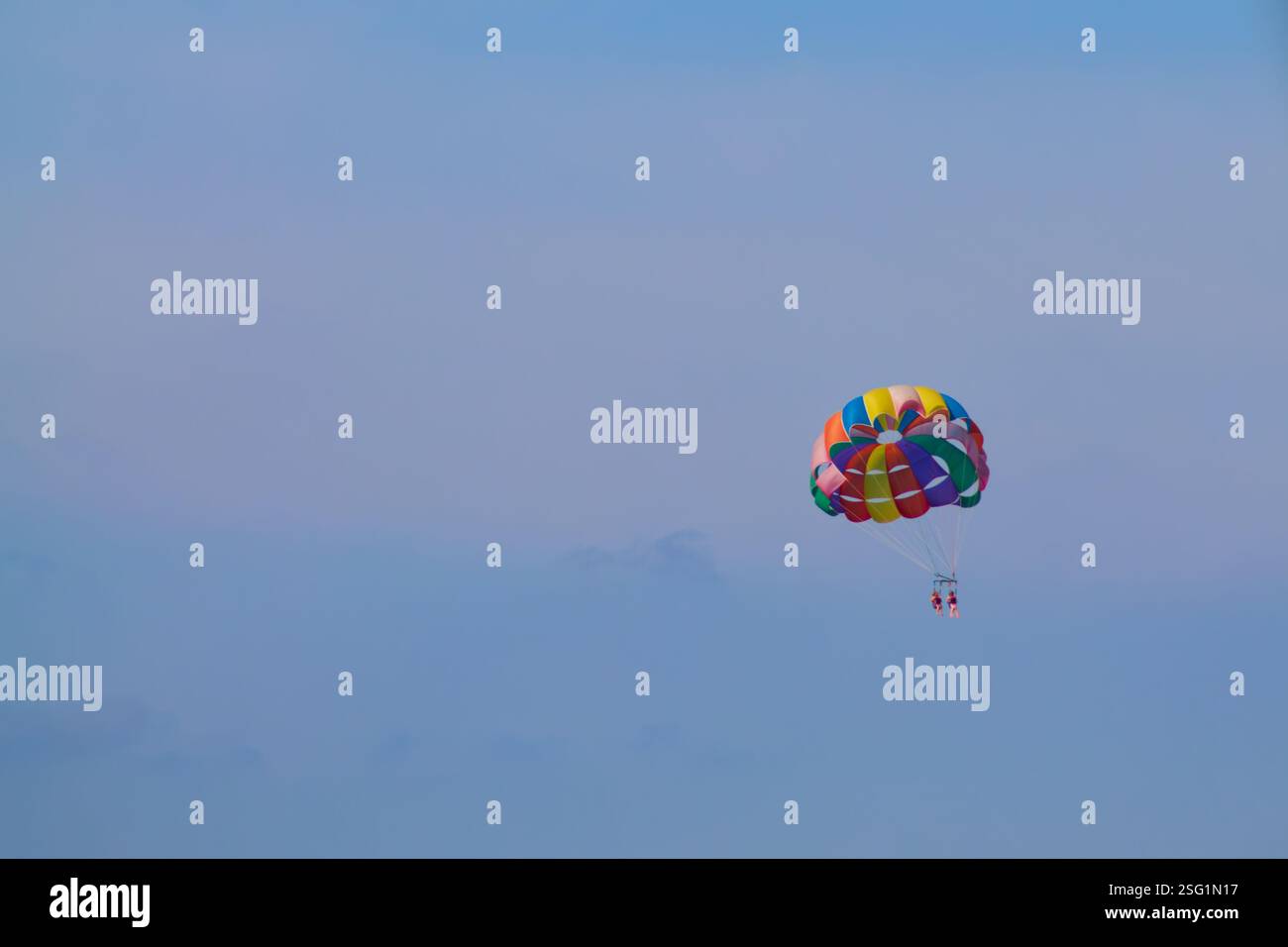 A colorful parasail soaring high in the sky, with two people enjoying ...