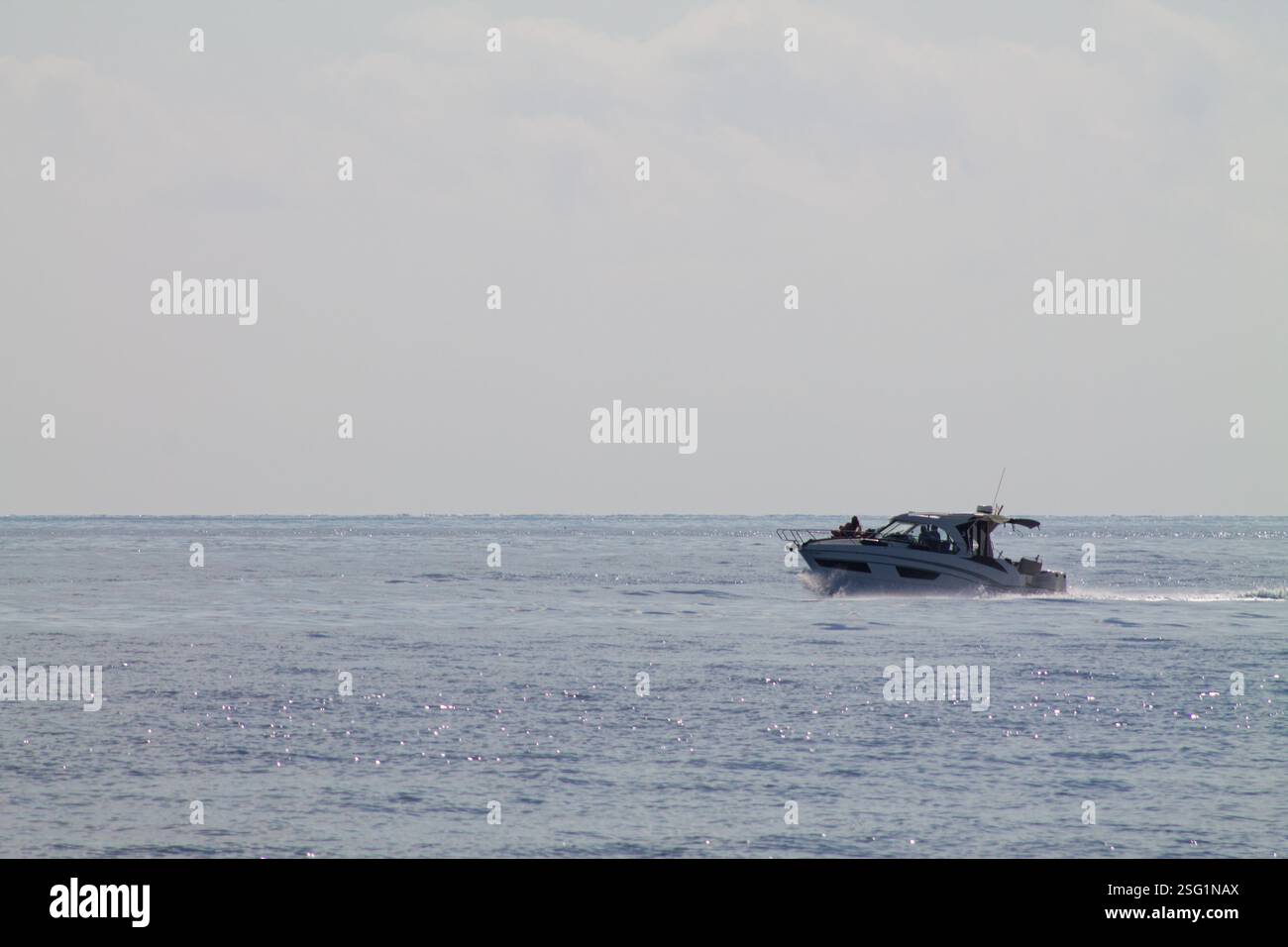 A motorboat cruising on calm ocean waters under a hazy sky. The boat ...