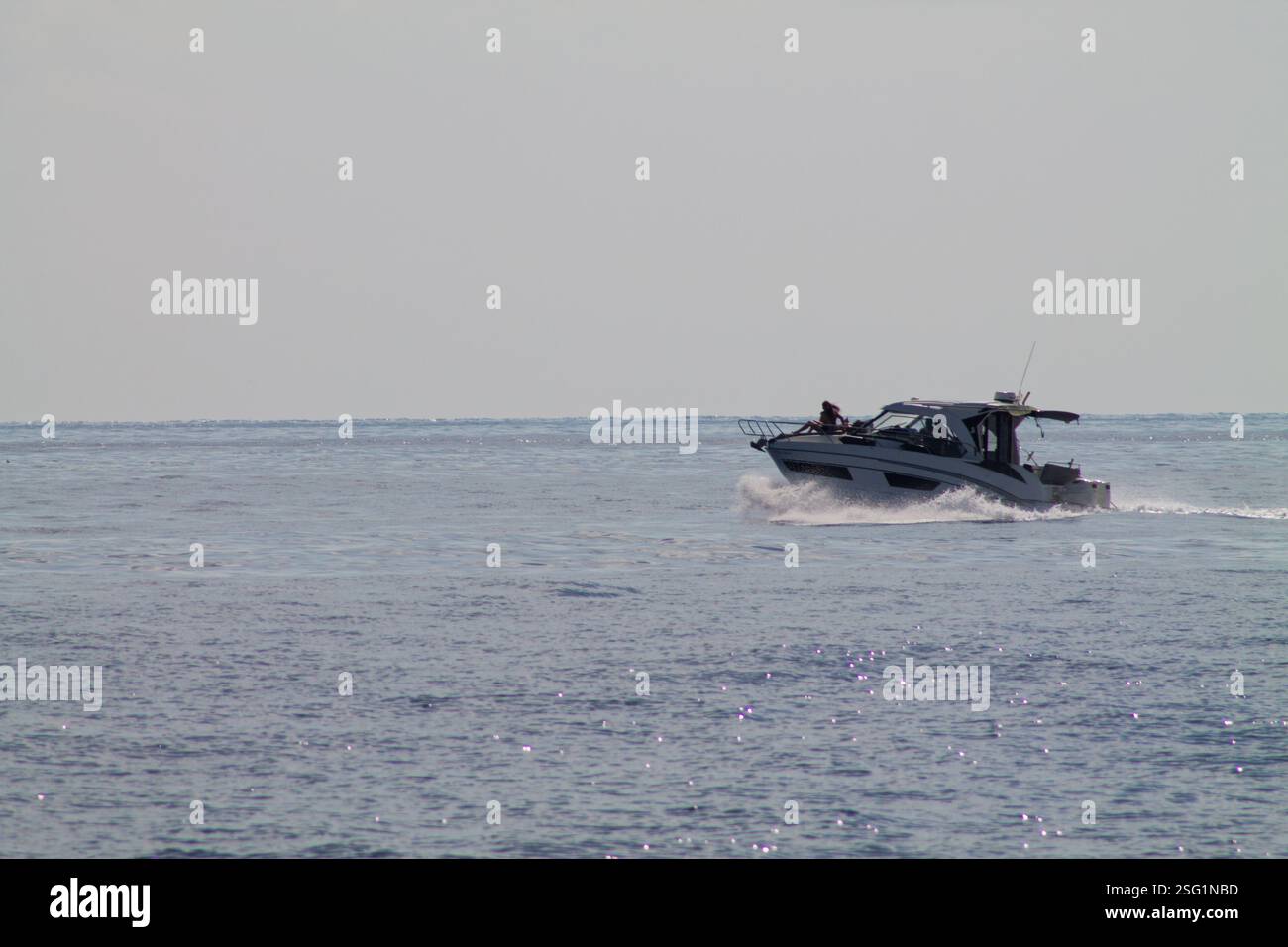 A motorboat cruising on calm waters under a hazy sky. The boat creates ...