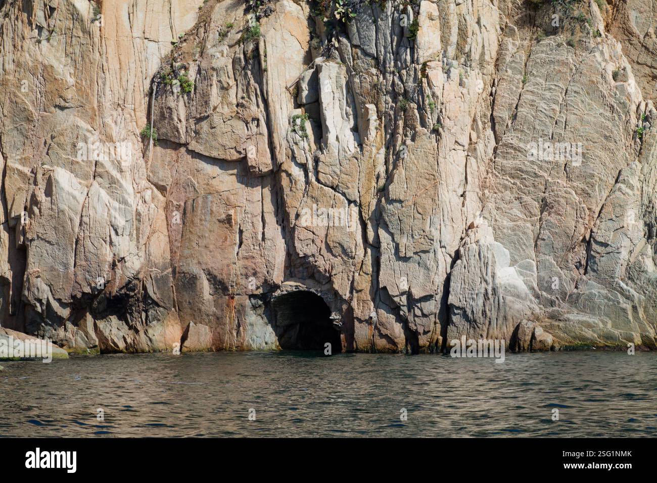 A rocky cliff face with a natural archway partially submerged in water ...