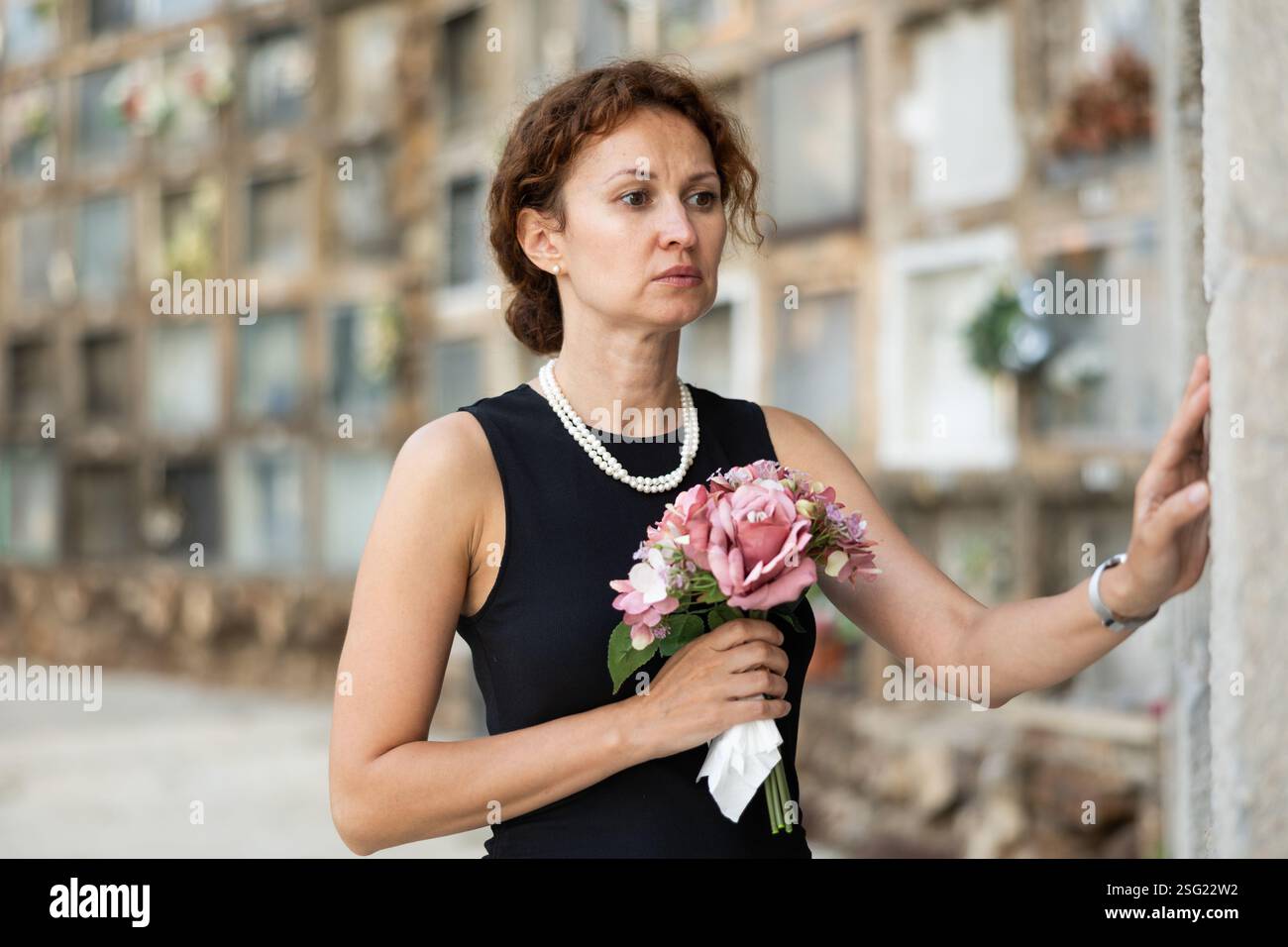 Grieving woman in black standing with bouquet near columbarium Stock ...