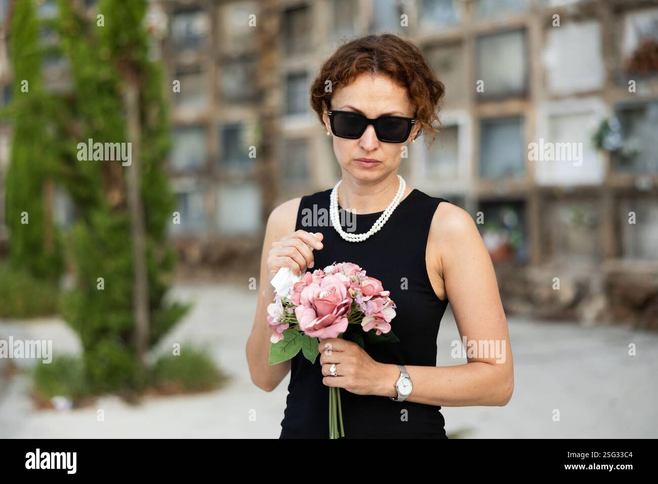 Grieving woman in sunglasses standing with flowers in cemetery Stock ...