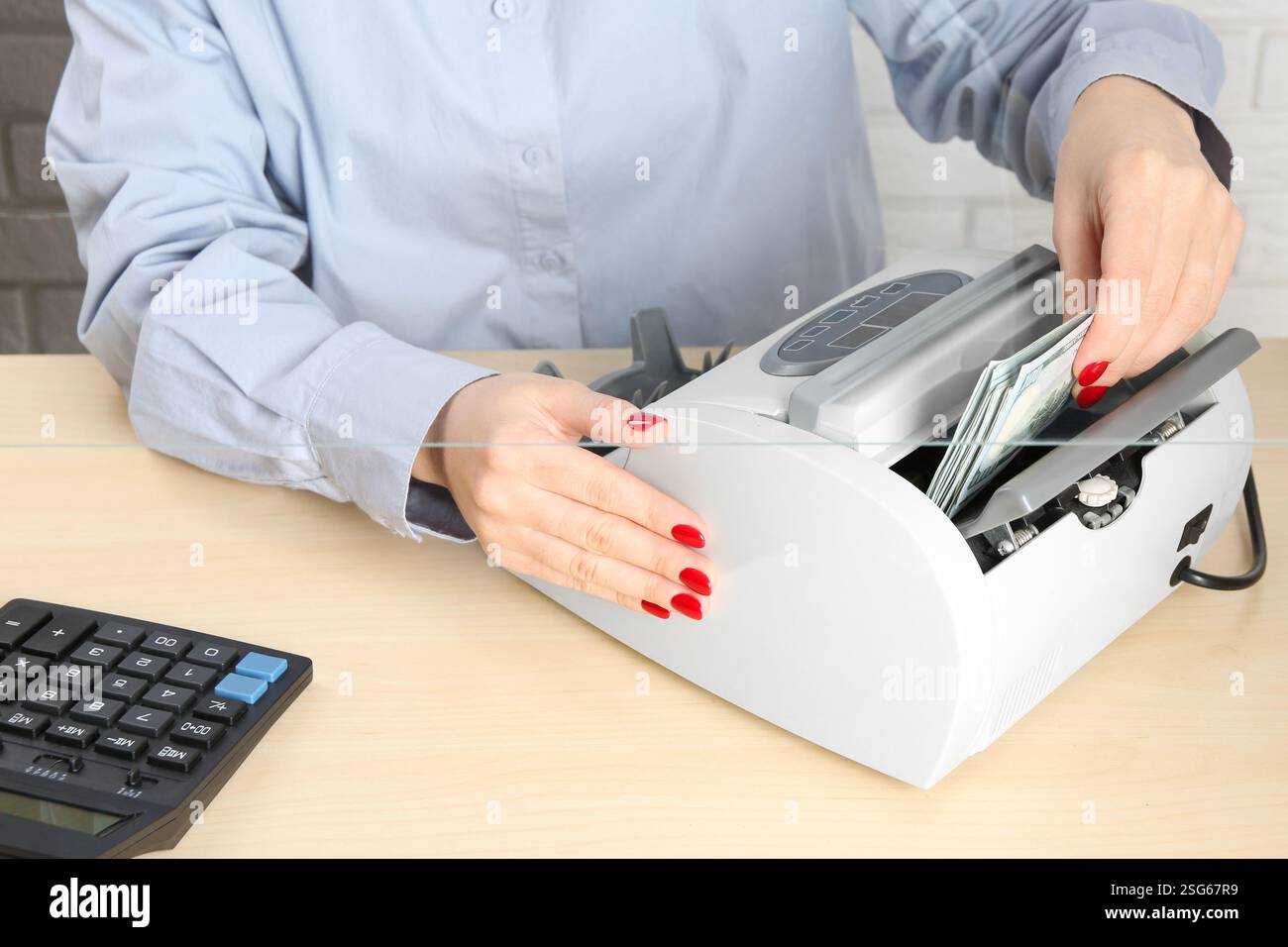 Cashier using money counting machine at table in currency exchange ...