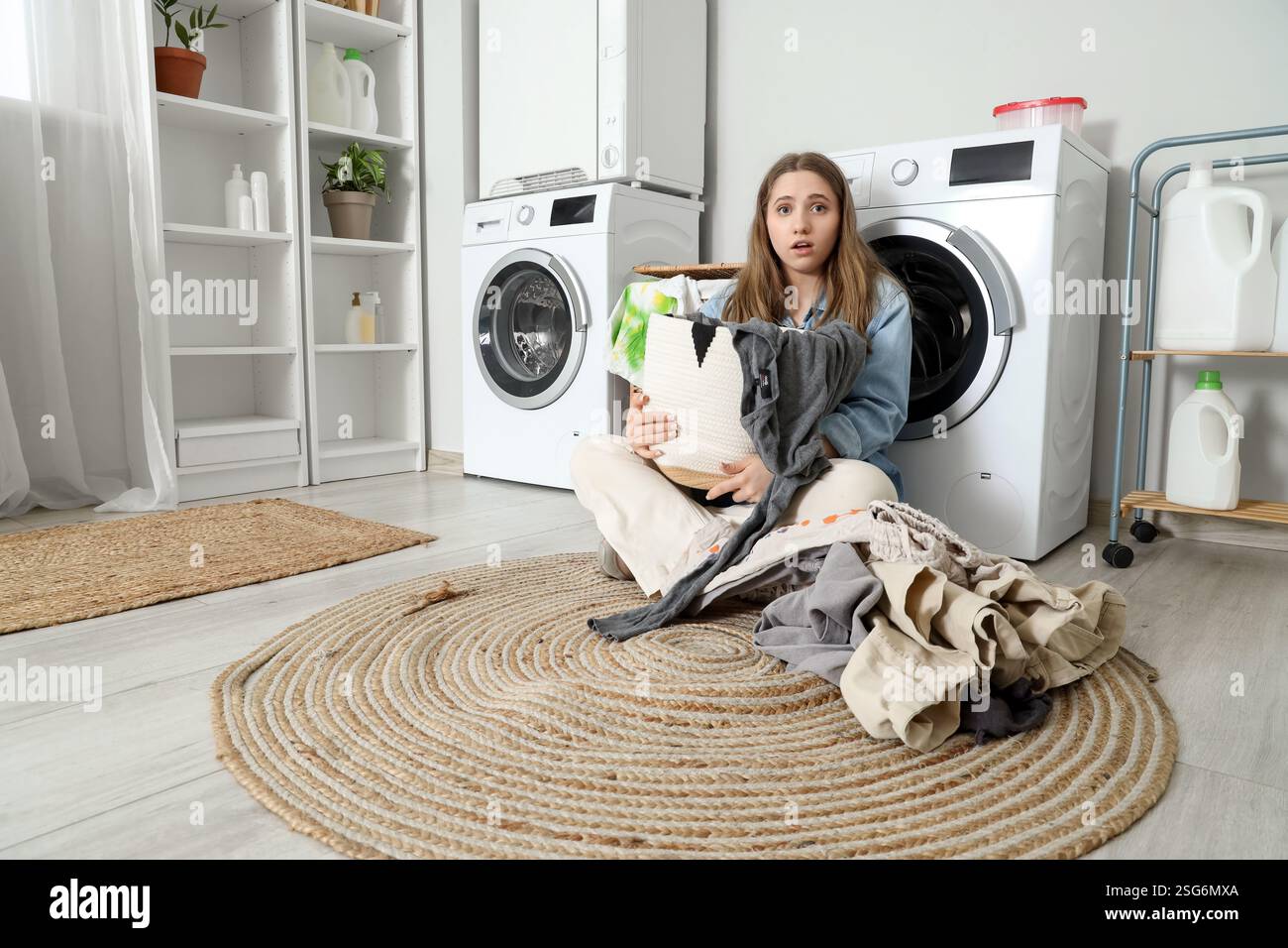 Shocked young woman sorting dirty clothes in laundry basket at home ...