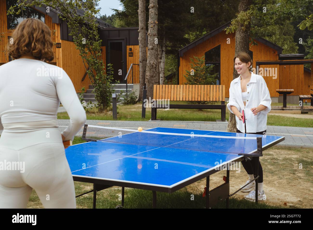 Two women engage in active game of ping pong at an outdoor table tennis ...