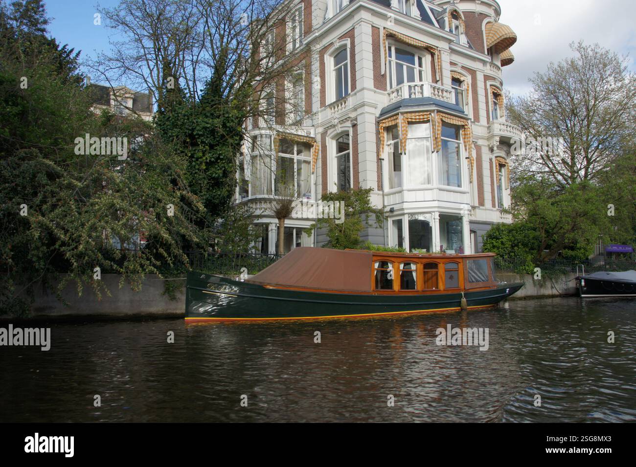 A houseboat floats on a scenic Amsterdam canal lined with trees. The ...
