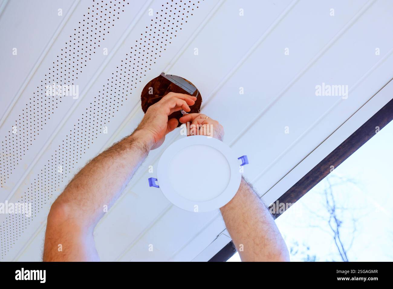 Hands are fixing an LED ceiling light fixture in brightly lit soffit ...