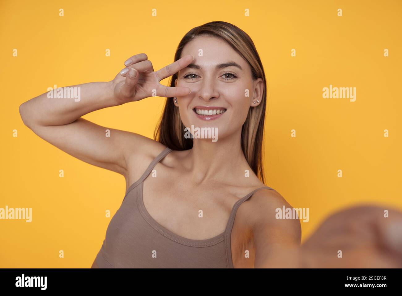Portrait of smiling woman giving peace sign gesture while looking at ...