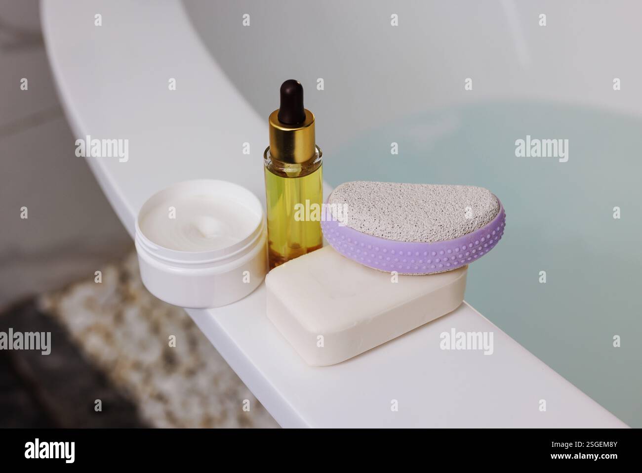 Spa essentials on bathtub edge: moisturizing cream, body oil with ...