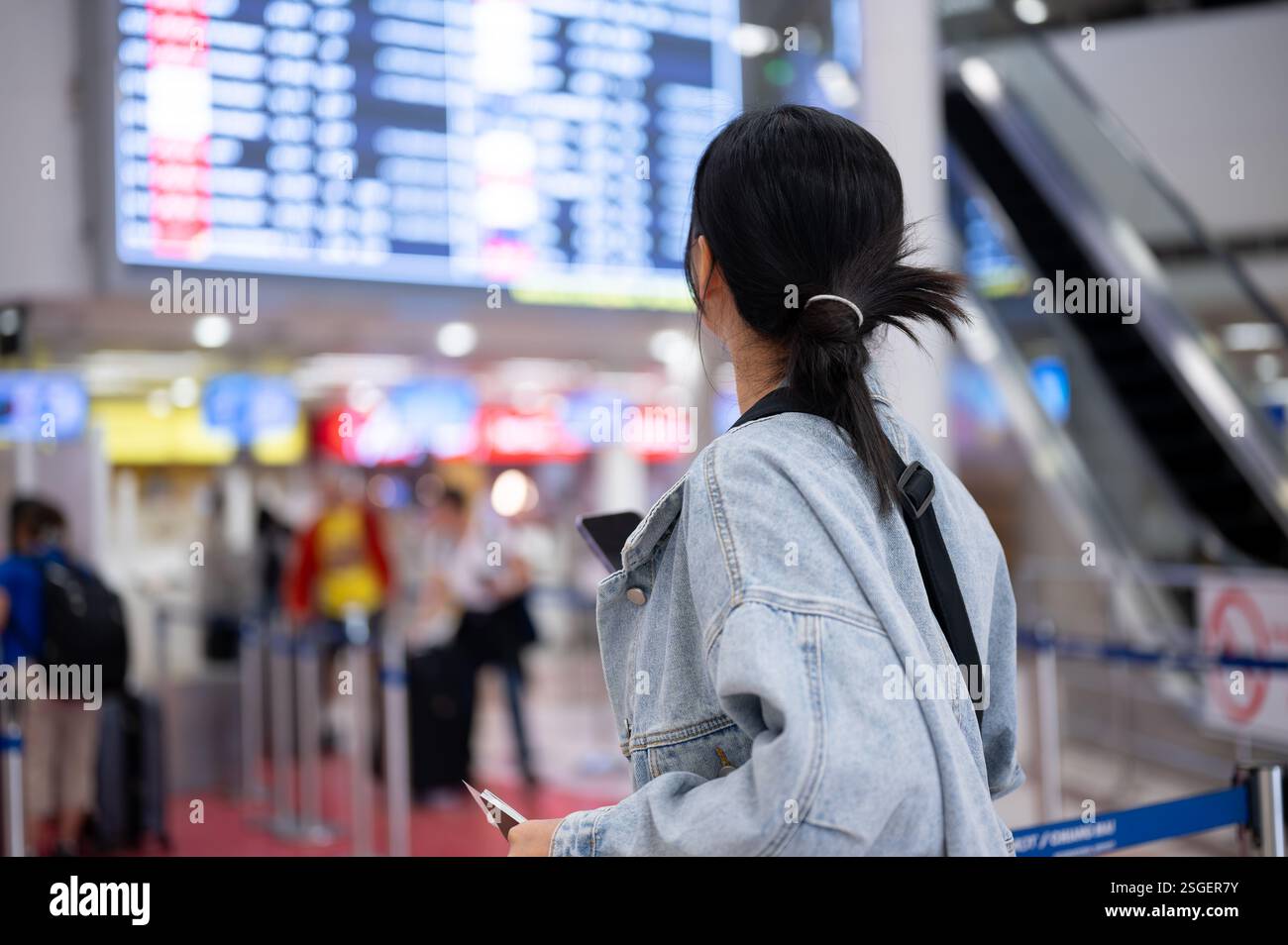 A back view of an Asian female passenger looking at a flight ...