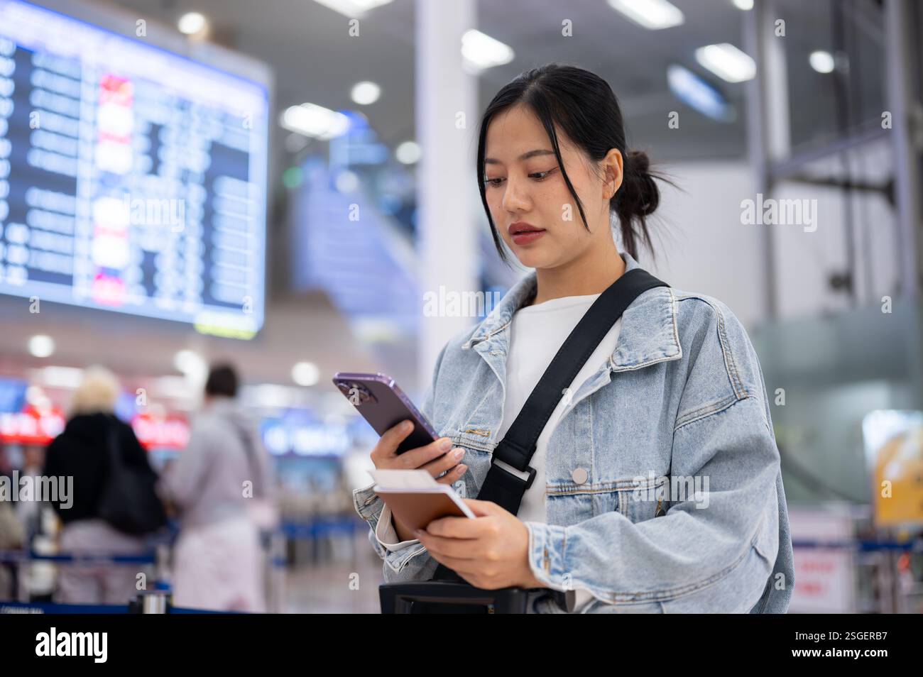 A positive, thoughtful Asian female passenger checks her flight boarding time on her smartphone ...