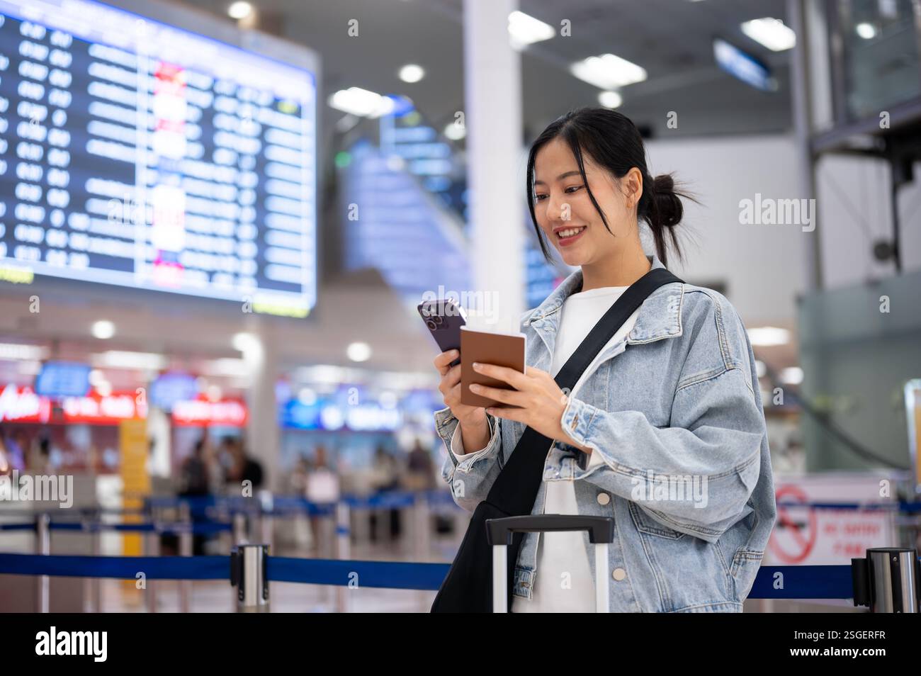 A happy Asian female passenger checks her flight boarding time on her ...