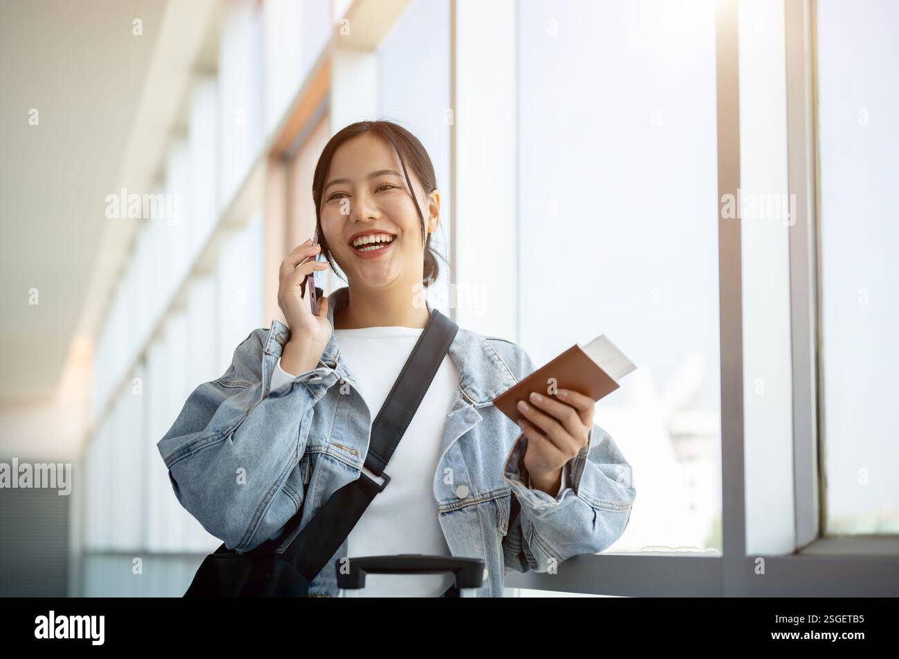 A cheerful, excited Asian female passenger enjoys talking on the phone ...