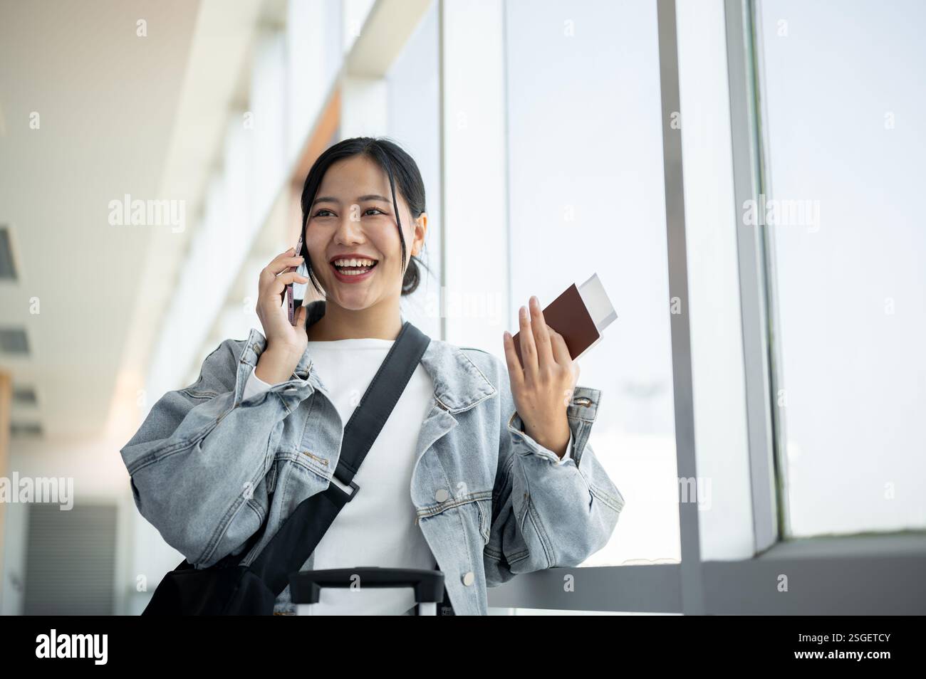 A cheerful, excited Asian female passenger enjoys talking on the phone ...