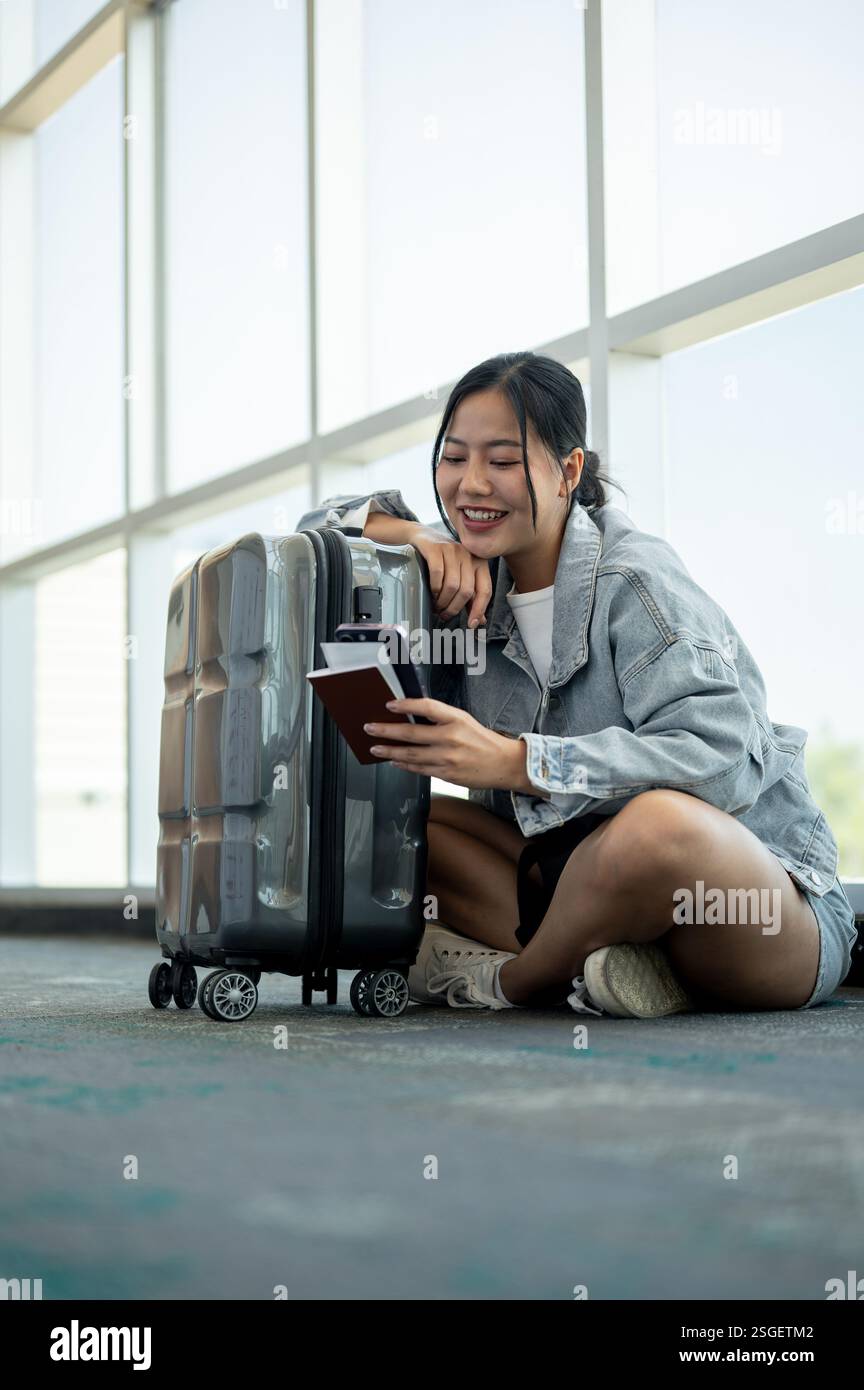 A positive, happy Asian female passenger sits on the floor beside her ...
