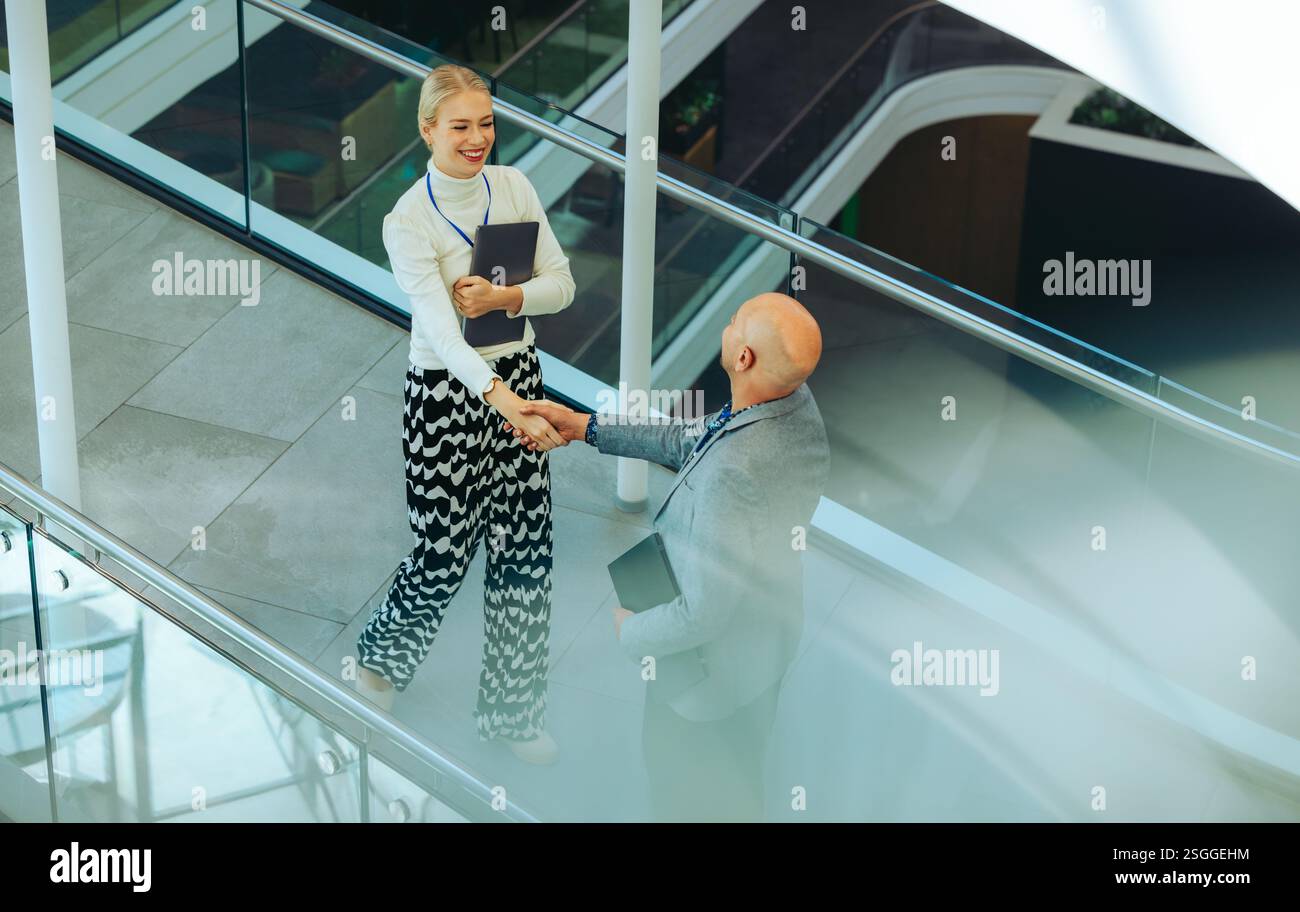 Two professionals in a modern office setting exchange a warm handshake ...