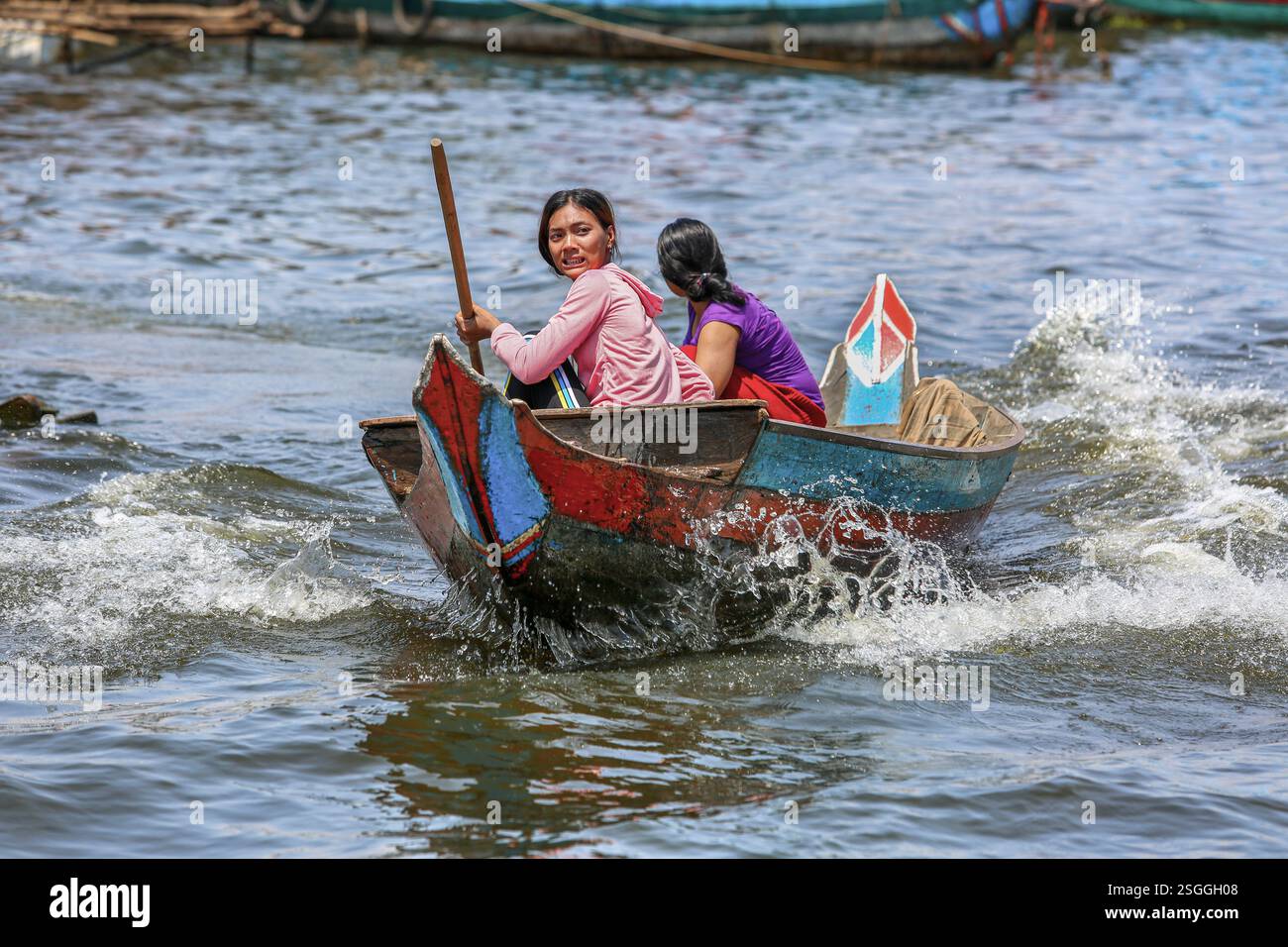 Cambodian women struggle with oars on traditional colorful boat against ...