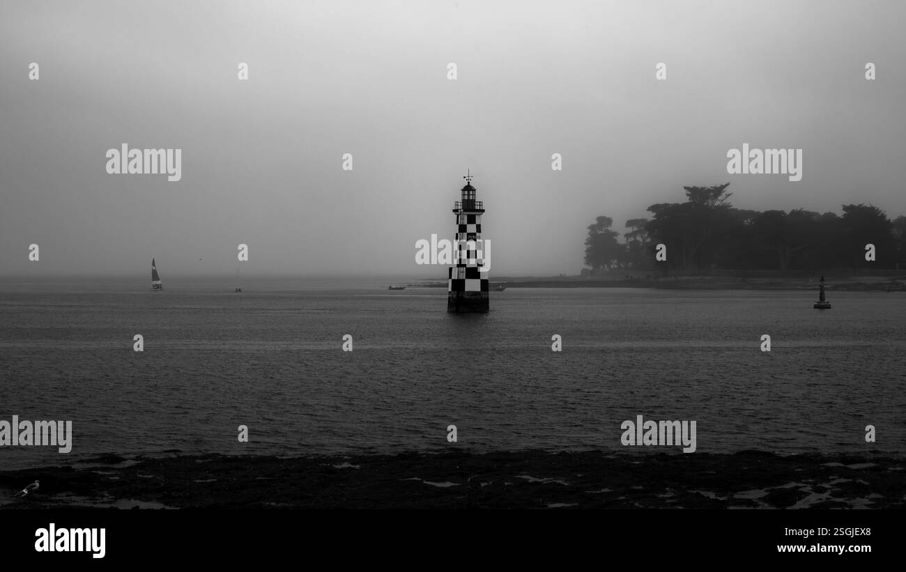 Monochrome photo of a lighthouse in the mist on the coast of Brittany ...