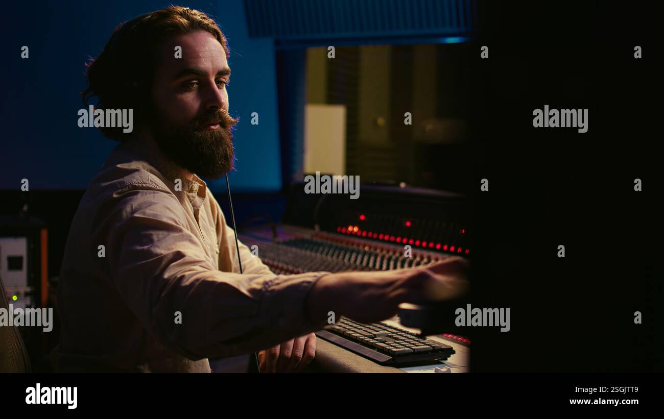 Audio expert operating motorized faders and mixing console in control room, using sliders and ...