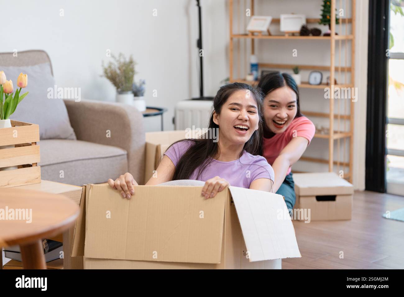 Diverse female couple having fun sliding in moving boxes while ...