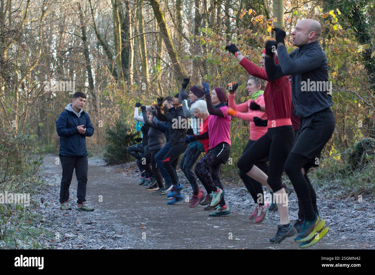 A group of people performing outdoor exercises on a forest path, with a ...