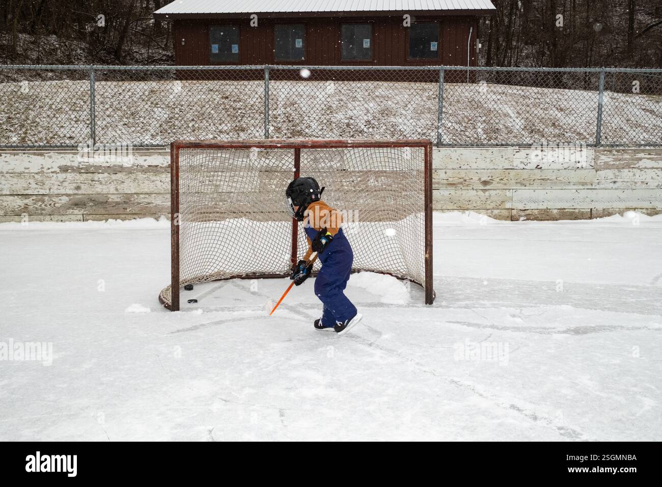 Child playing hockey on an outdoor snowy rink by a rustic fence Stock ...